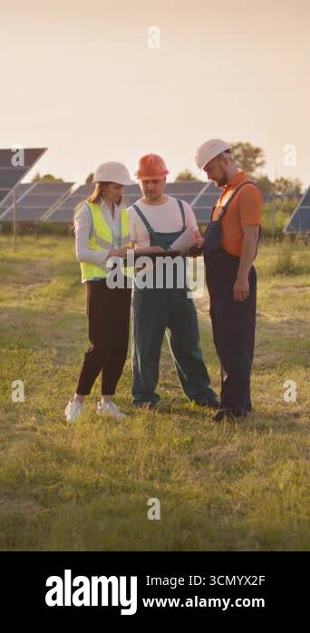 A team of engineers and workers discuss plans in front of a solar panel ...