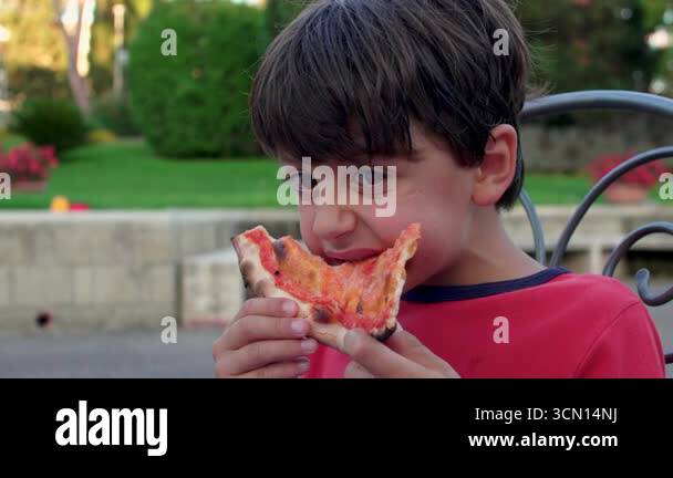 Young boy in red shirt holding slice of pizza with both hands, playful ...
