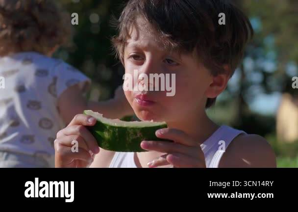 Closeup of young boy biting into watermelon rind outdoors, wide eyed ...