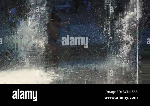 Boy running joyfully through water fountain jets with spray splashing ...