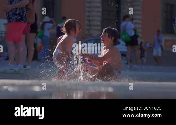 Two children laughing and splashing together in fountain, carefree ...