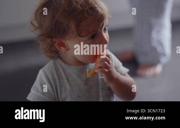 Toddler eating fresh fruit while standing in kitchen, candid moment of ...