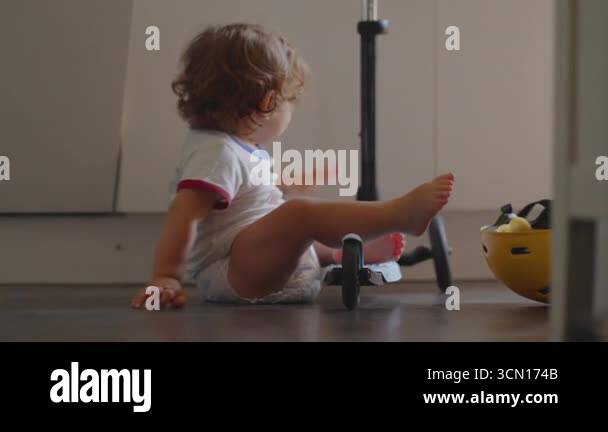 Toddler sitting on kitchen floor reaching for scooter handle, playful ...