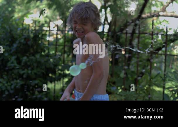 Boy getting hit by flying water balloon in backyard summer battle, slow ...