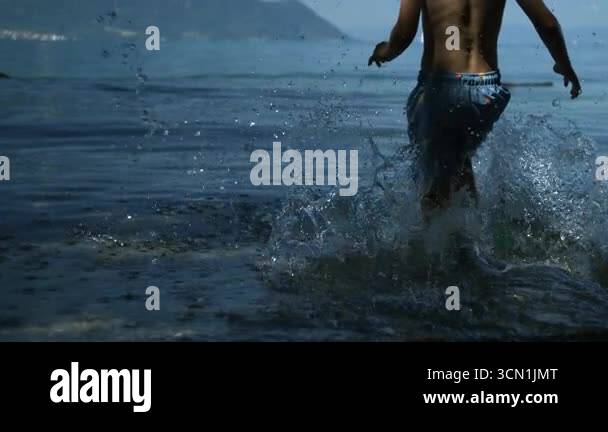 Boy running into lake slow motion, water splashing around legs, playful ...