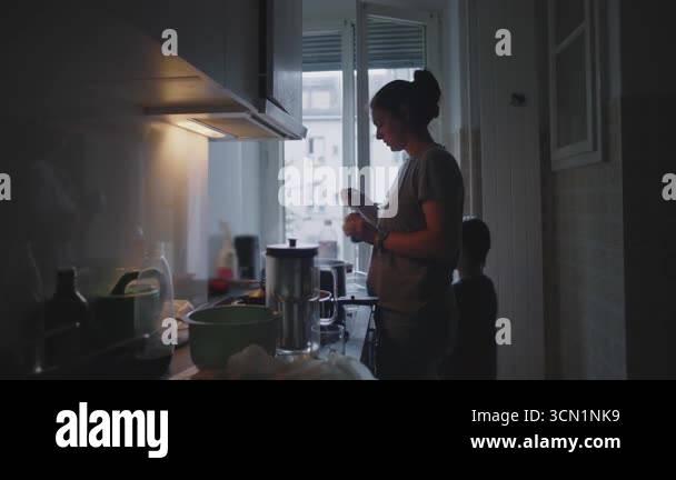 Mother cooking dinner in kitchen while holding toddler nearby, stirring ...