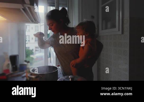Mother multitasking in kitchen tasting food from steaming pot while ...