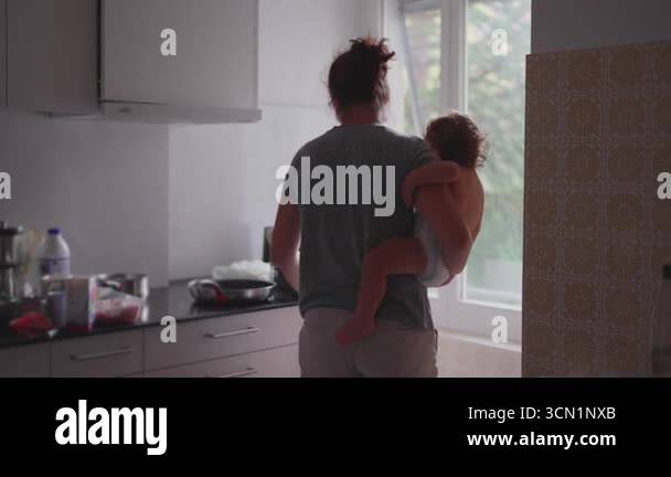 Mother cooking in kitchen while holding small child, multitasking ...