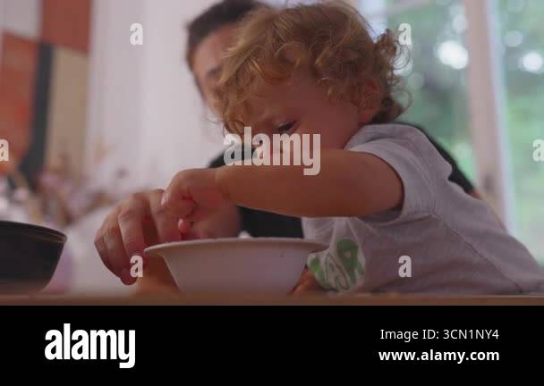 Toddler sitting at dining table, gazing thoughtfully at bowl while ...