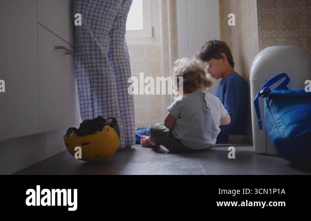 Toddler sitting on kitchen floor with older brother while mother cooks ...