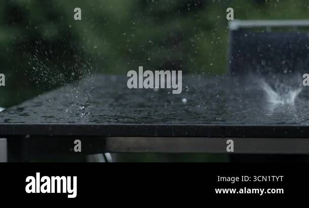 Close up of rain hitting table surface and exploding into droplets in ...