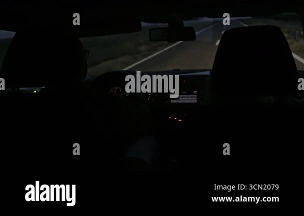 video taken from inside a moving car at night. The driver is seen ...