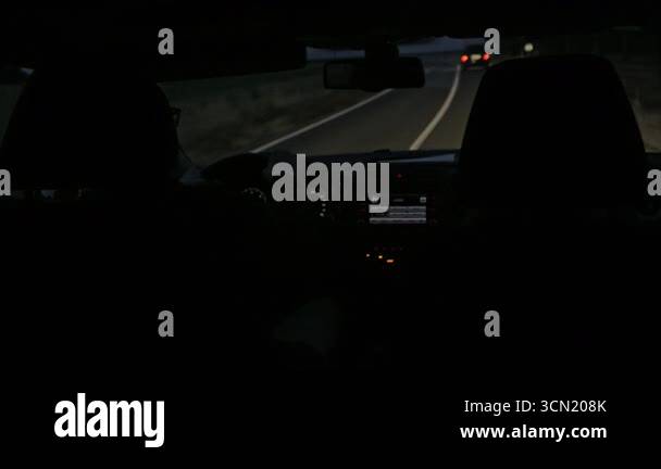 A dimly lit car interior with a driver steering through a deserted ...