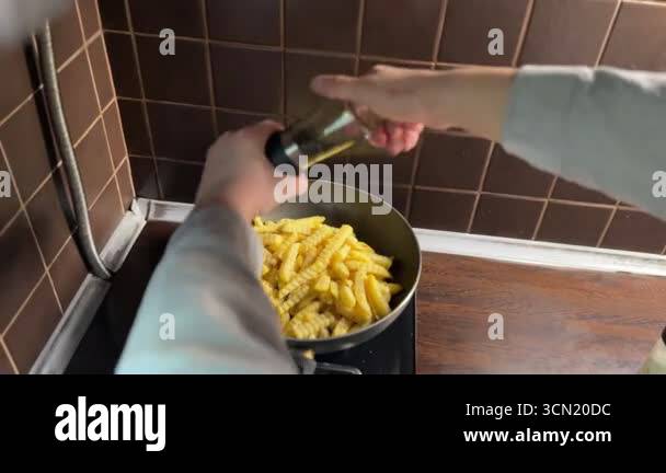 Close up of a person seasoning hot french fries in a frying pan using a ...