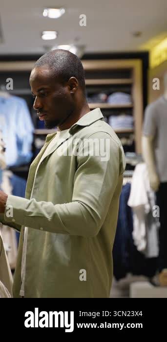 Young male carefully examining beige pants on hanger, displaying ...