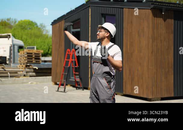 Construction worker wearing uniform, hard hat, and gloves explains something while pointing to ...