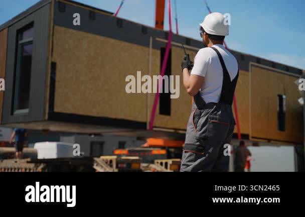 Construction professional wearing protective gear, coordinating modular house installation using ...