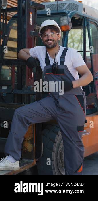 Confident warehouse worker in safety gear standing near forklift ...