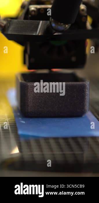 3D printer working, printing detail a square piece with black filament ...
