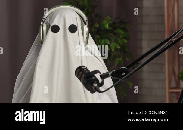 A person dressed as a ghost, wearing a white sheet and headphones, sits ...
