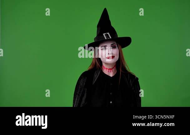 A witch with vampire makeup, in a black cloak and hat, blows a kiss ...