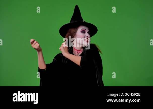 A witch with vampire makeup, in black cloak and hat, dances cheerfully ...