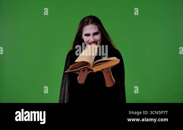 A female witch with vampire makeup and a black cloak casts spells over ...