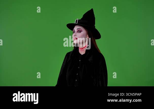 A witch with vampire makeup, in a black cloak and hat, makes a ...