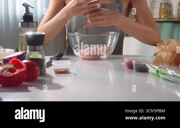 A woman sprinkles salt, pepper, and various spices on sliced chicken ...