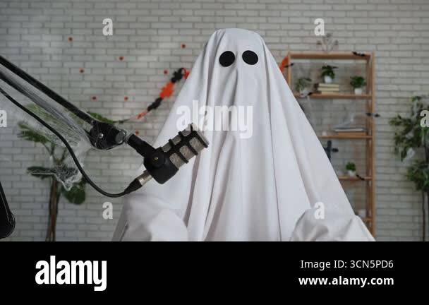 A person dressed as a ghost, wearing a white sheet, sits in front of a ...
