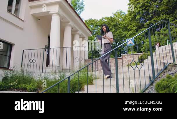 Confident Caucasian young woman going down the stairs near modern old ...