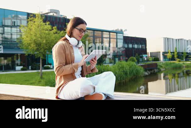 Young woman sitting cross-legged on bench in urban outdoor park ...