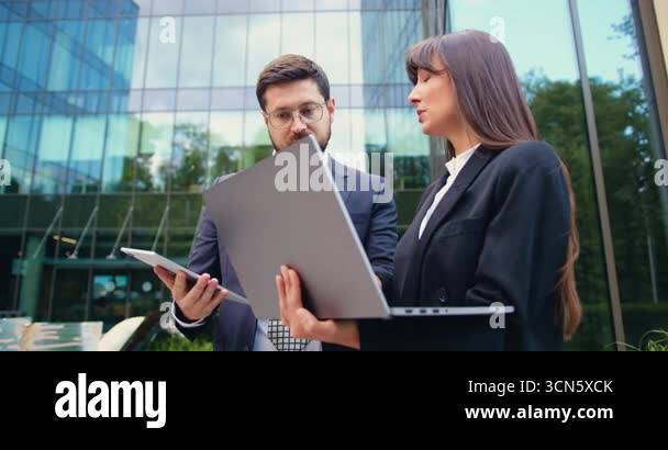 Two business professionals in formal attire standing outdoors ...