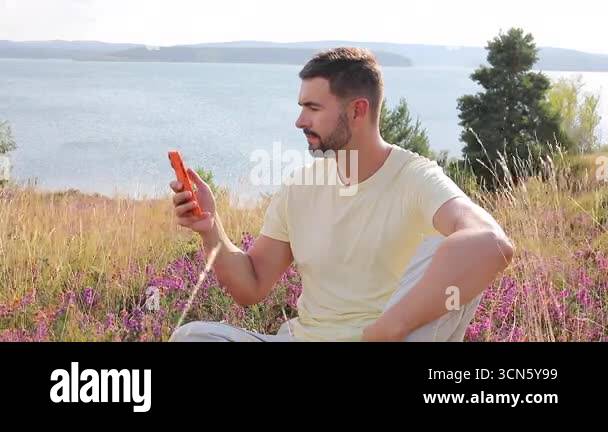 happy man using smartphone while sitting on grass on hill Stock Video ...