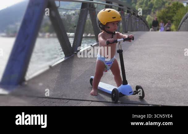 Toddler standing on scooter wearing yellow helmet, little child paused ...