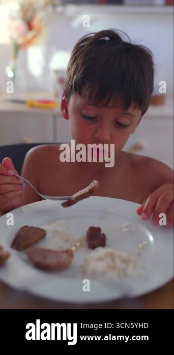 Young boy eating meat and rice at home, holding fork and tasting food ...