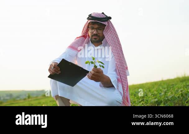 Arab agronomist, wearing traditional attire and glasses, squats in a ...