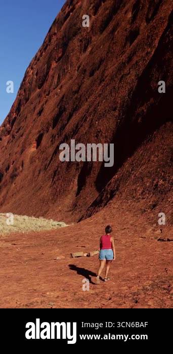 A woman walks along the sunlit, textured base of Uluru, Australia's ...