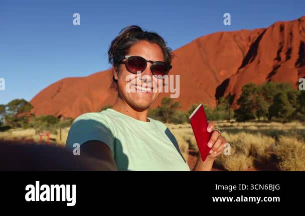 A woman stands smiling while holding a passport at Uluru, Ayers Rock in ...