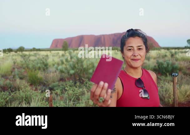 A woman holding a passport obscures her face in an open field, with the ...