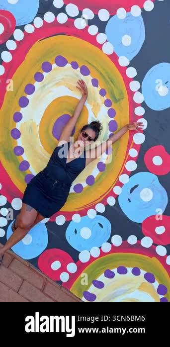 A smiling woman stands with arms outstretched in front of a vibrant ...