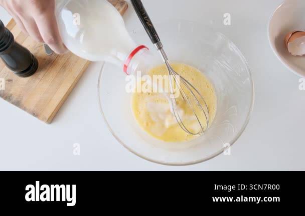 Man pouring milk and whisking beaten eggs in glass bowl in light ...