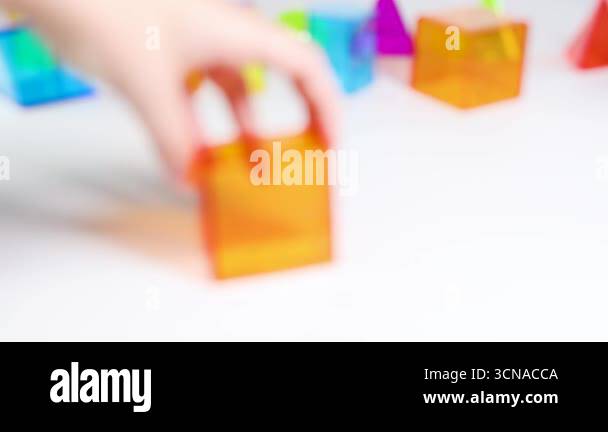 Hands manipulate vibrant 3D geometric shapes on a white surface ...
