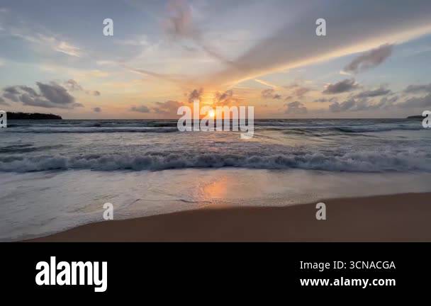 Golden sunset over the ocean with rolling waves crashing onto the sandy shore, reflecting warm ...