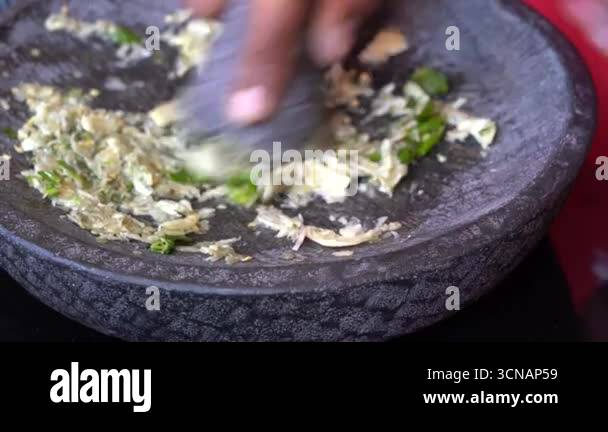 Grinding garlic and green pepper with mortar and pestle, close up ...