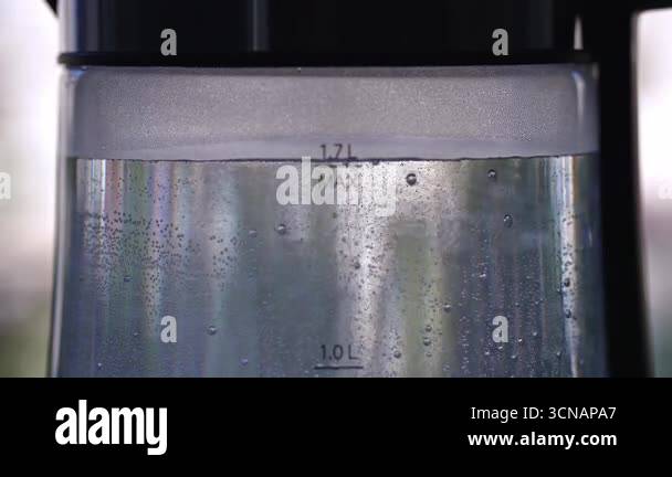 Boiling water in glass kettle, closeup macro view, bubbles rising ...