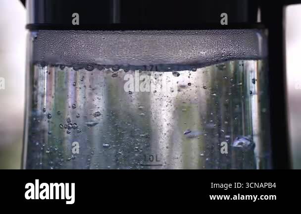 Boiling water in glass kettle, closeup macro view, bubbles rising ...