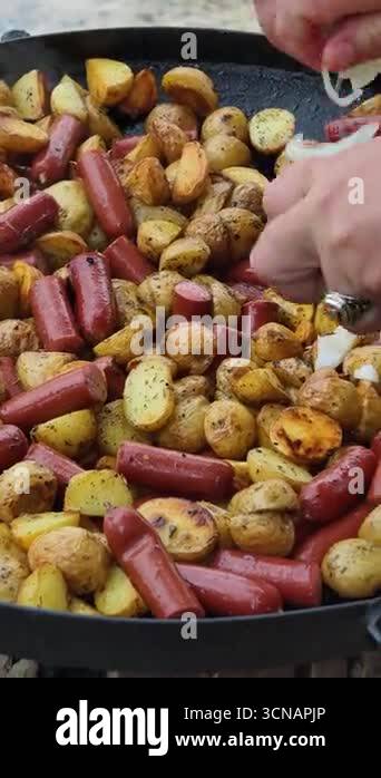 Top-down view of a hand spreading sliced onions over frying potatoes ...