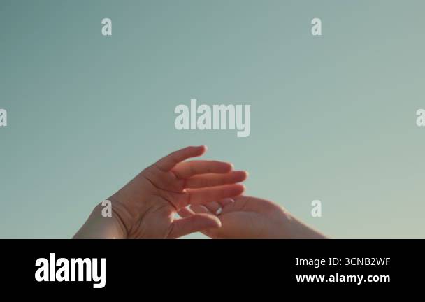 Artistic close-up image of two hands raised against a clear blue sky ...