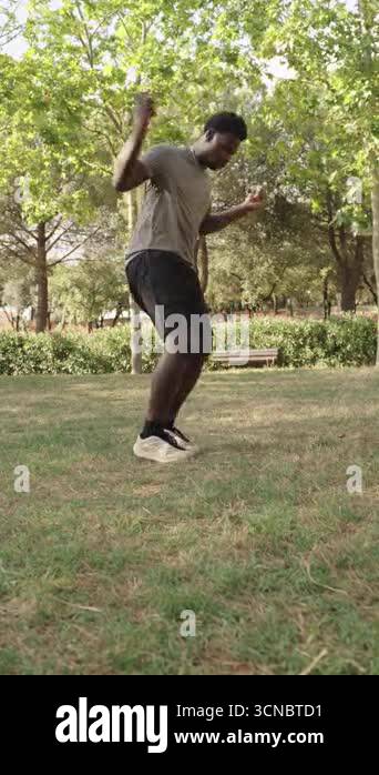 Male athlete demonstrating high energy jump rope workout in lush park ...